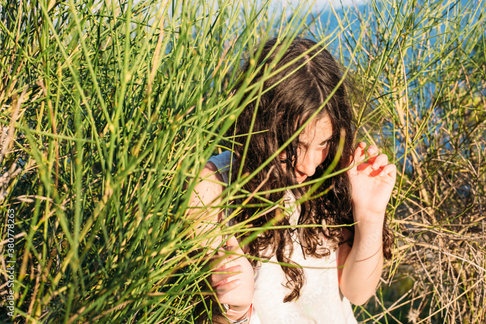 Preteen girl among the dense bush of the forest, with the sea in the ...