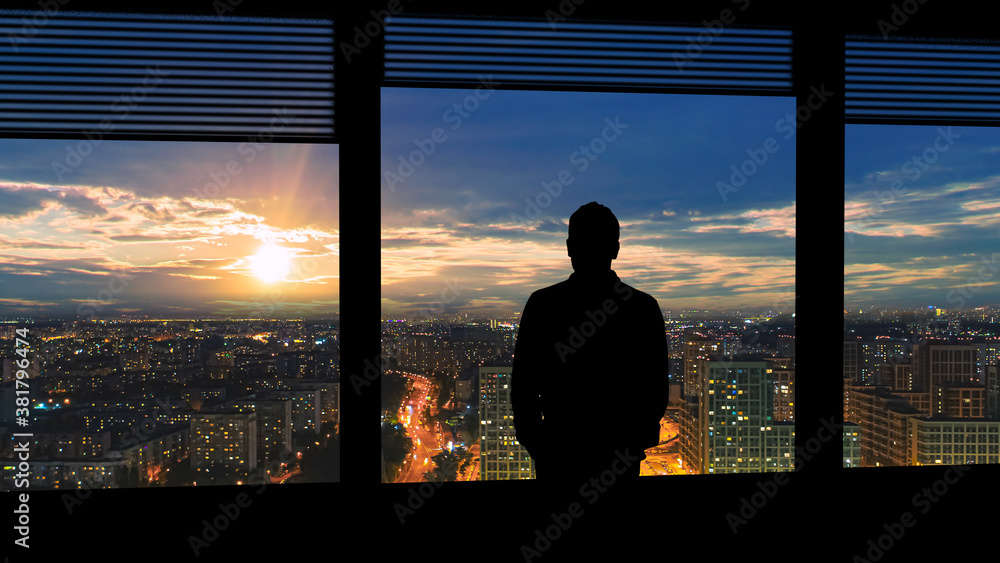 The lonely man standing near the window on the night city background ...