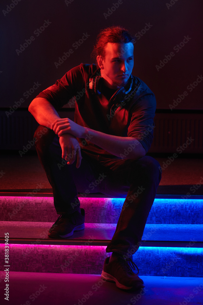Young computer programmer in headphones sitting on illuminated stairs ...