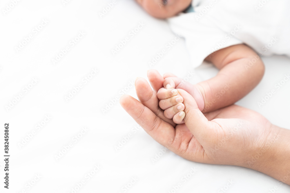 Newborn baby holding mother’s finder while sleeping on white bed ...