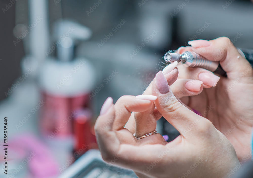 Girl doing her nails herself, using nail milling machine for drilling ...