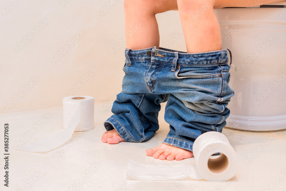 Using toilet. Woman uses a toilet with jeans around ankles in bathroom ...