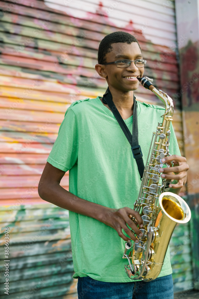 Black teenager practicing saxophone at school on colorful background ...
