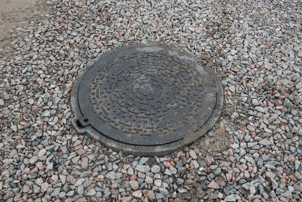 one black iron sewer manhole among gray fine rubble on the road outside ...