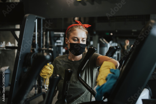 Young female worker disinfecting cleaning and weeping expensive fitness ...