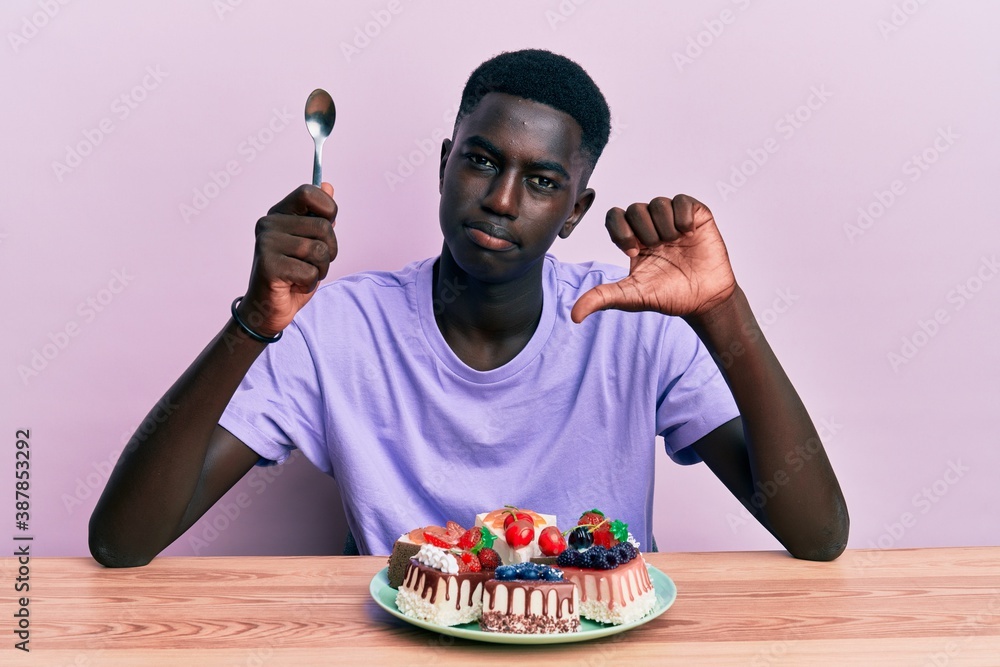 Young african american man sitting on the table eating cakes with angry ...