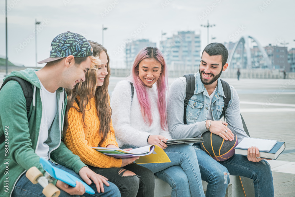 Multiethnic students joking and talking sitting on the bench together ...