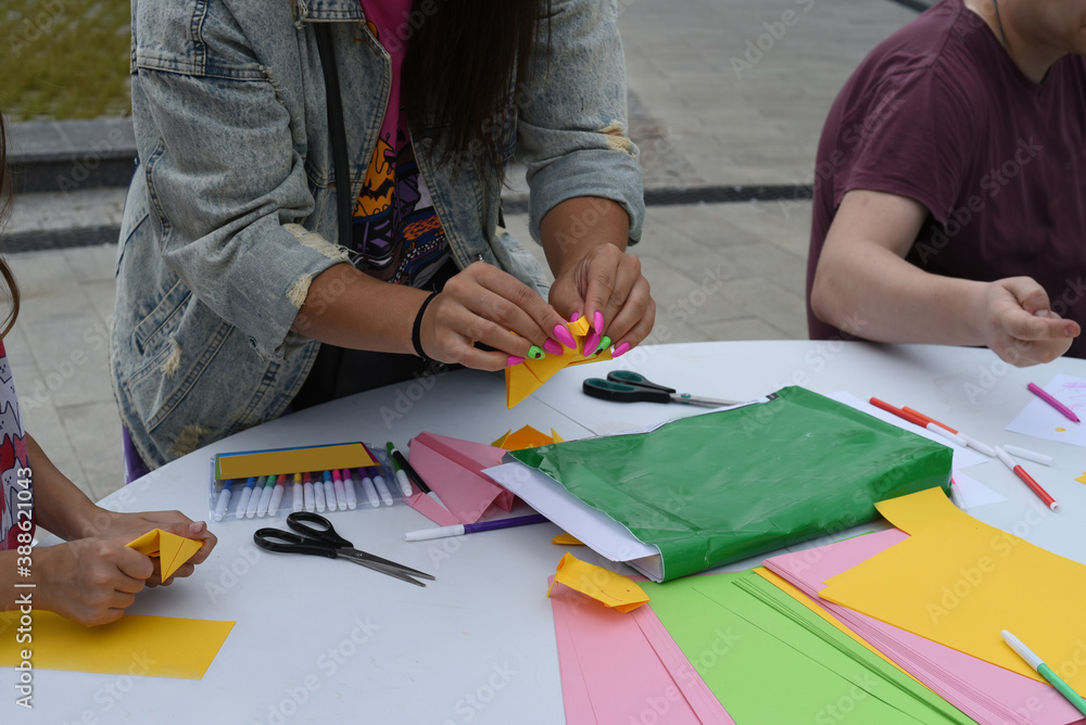 The girl shows a master class, making origami from a yellow sheet of ...