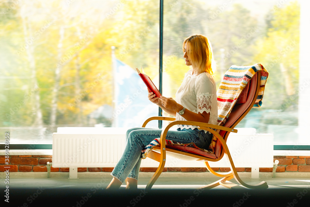 Young attractive woman swinging in a comfortable rocking chair reading ...