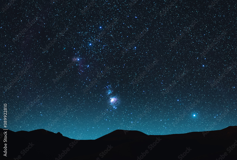 Beautiful Orion Nebula on the starry sky over the hill silhouette. Night photography ...