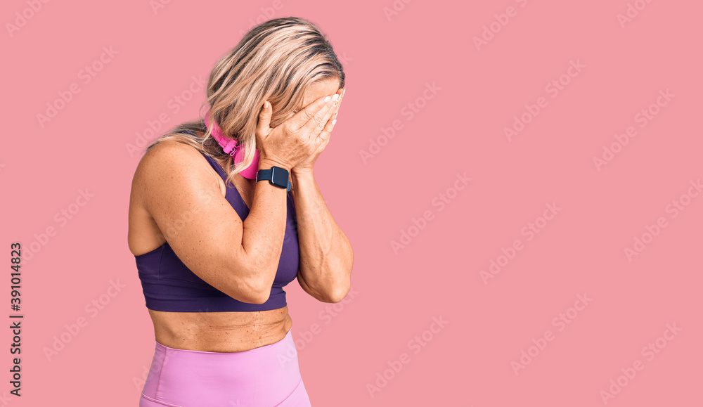 Middle age fit blonde woman wearing gym clothes and using headphones ...