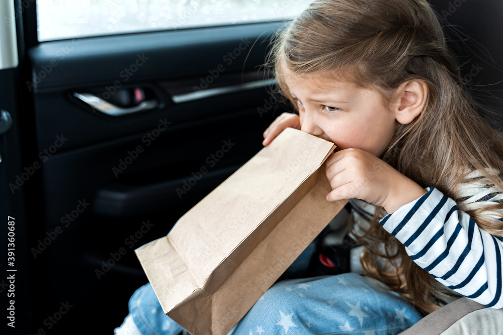 Little girl is driving in car. Kid is sick, feels bad and vomiting into ...