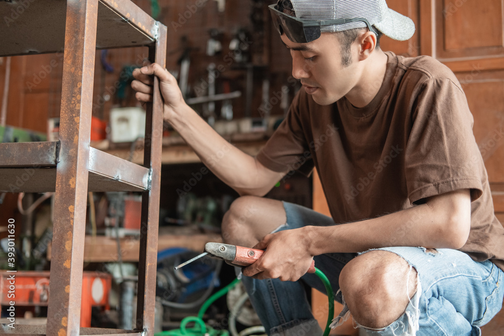 Asian welder holds an iron rack when welding using an electric welder ...