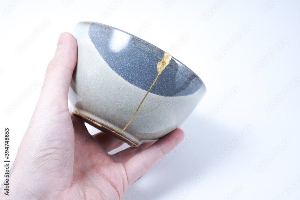 Hand holding kintsugi bowl. Gold cracks restoration on pottery restored ...