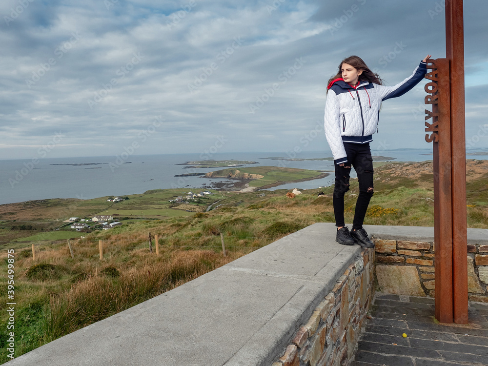 Young slim teenager tourist standing on a stone fence. One hand on Sky ...