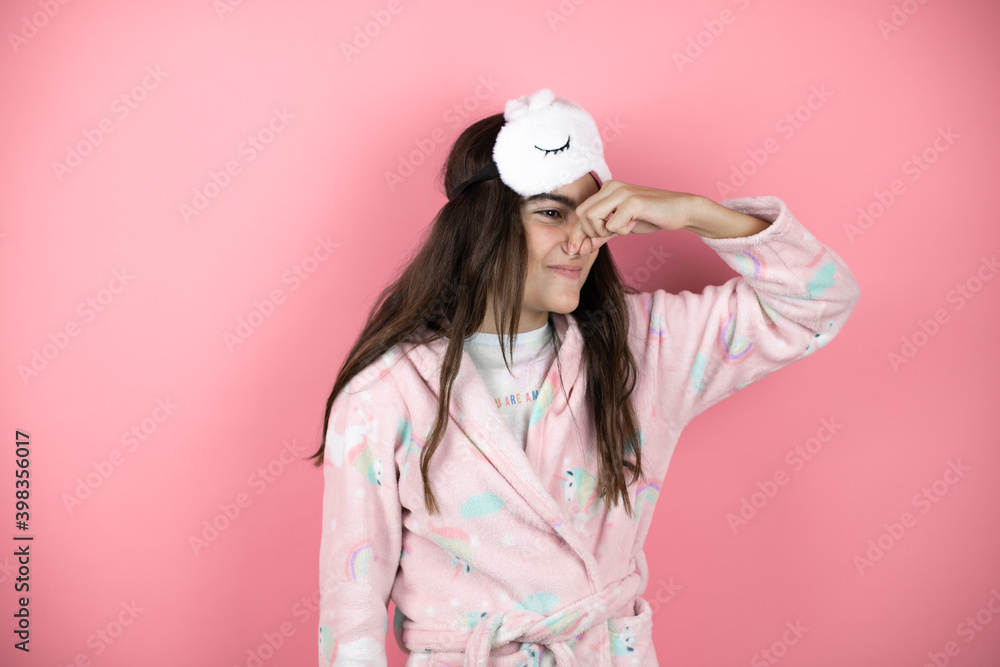 Pretty girl wearing pajamas and sleep mask over pink background ...