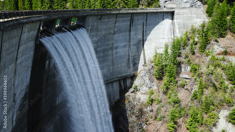 Water overflowing above an arched concrete dam built between two rocky ...