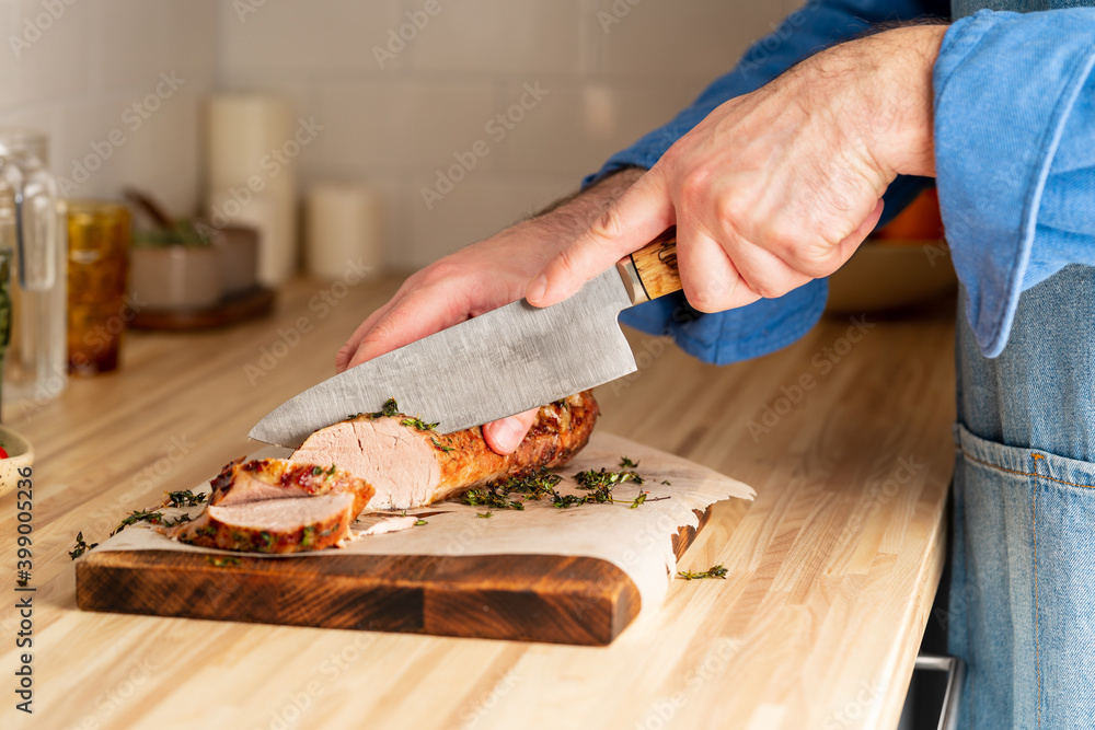 Unrecognizable man cuting with large knife baked pork tenderloin on ...