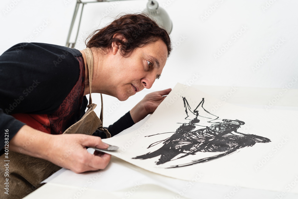 Side view of artisan female printmaker examining paper sheet with ...