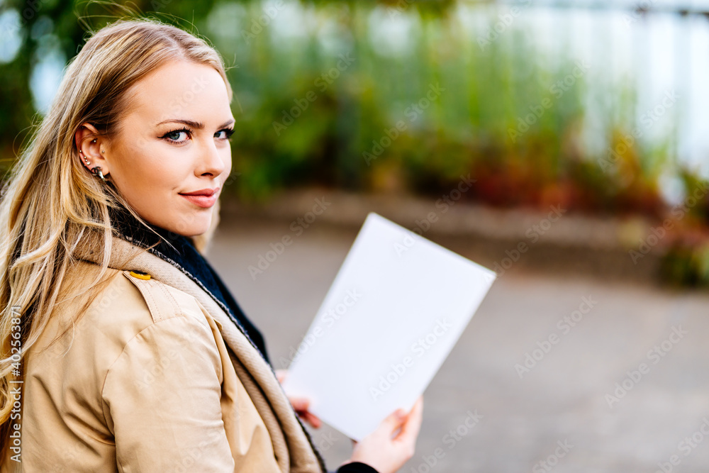 Young woman sitting on a park bench reading a magazine with a blank ...
