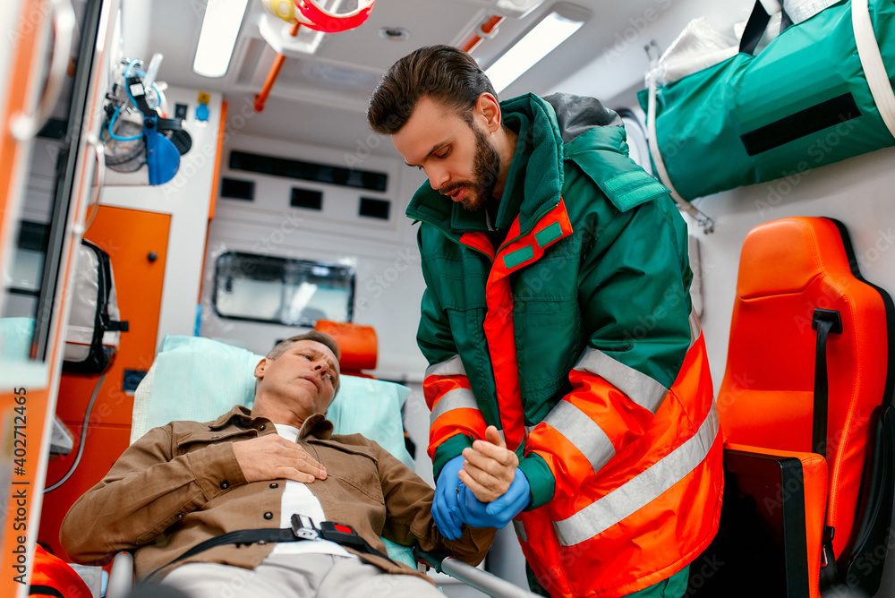 A male paramedic in uniform measures the pulse of a senior patient ...