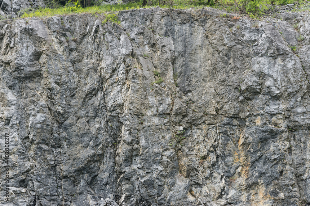 Weathered rock face texture in old stone pit with parts of green. Aged ...