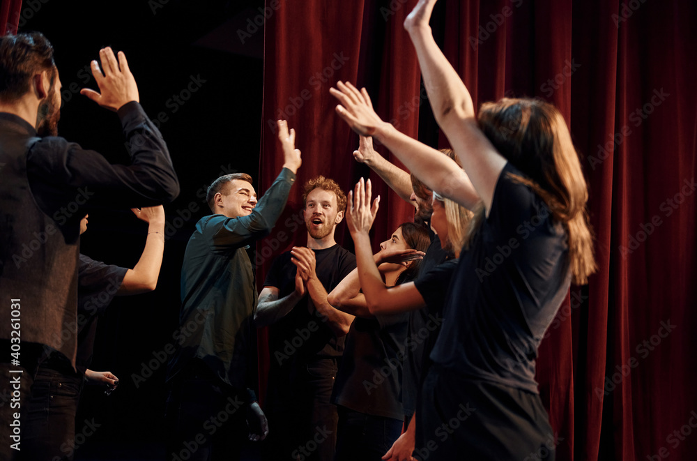 Giving high five, celebrating success. Group of actors in dark colored ...