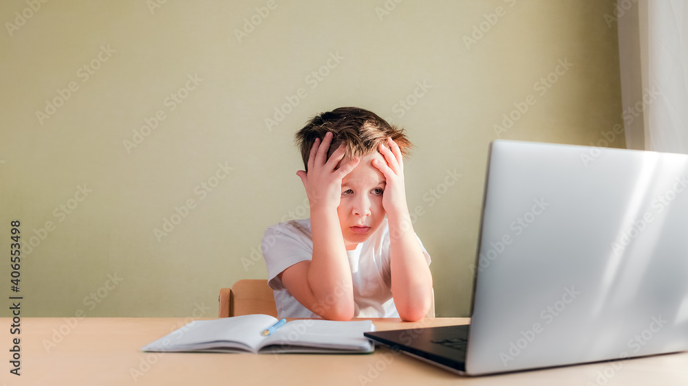 Desperate Child sits at a desk, looks sadly at the computer and holds ...