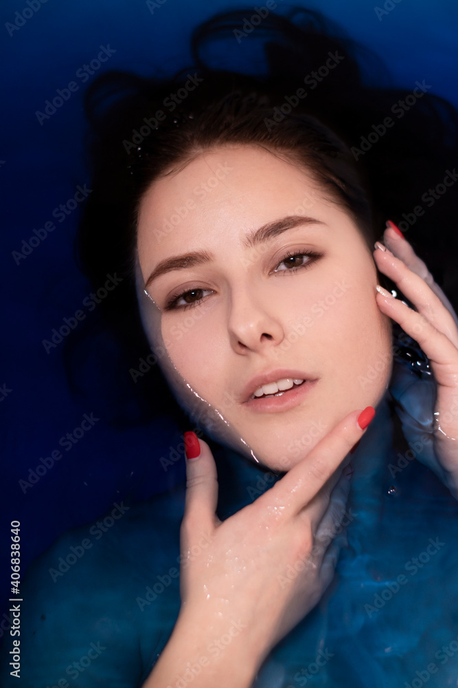 portrait of attractive brunette woman topless in blue liquid. in bathtub with colored water ...