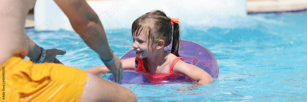 Little girl in pink lifebuoy swims to her father in the pool of water ...