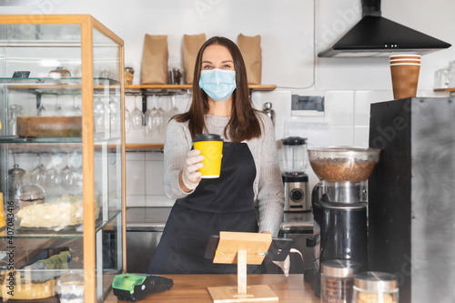 A female barista wearing protective mask and gloves giving a takeaway ...