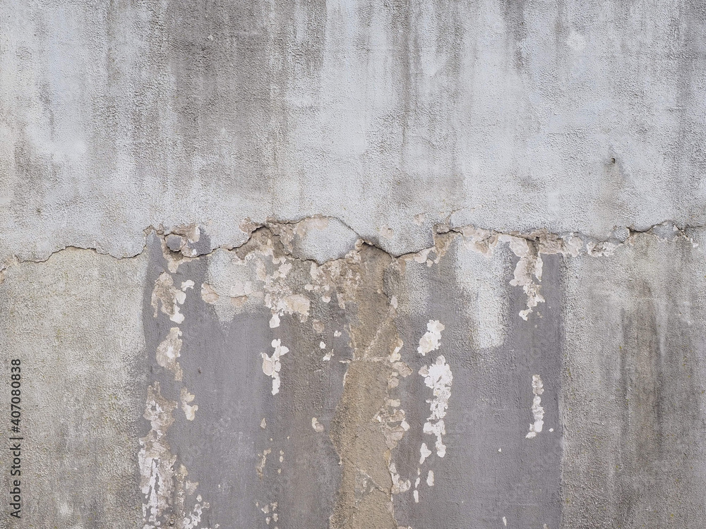 Gray concrete wall with a large transverse crack and peeling plaster ...
