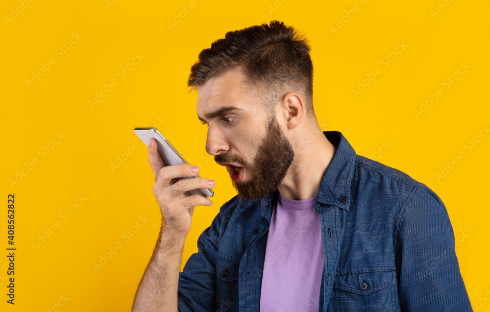 Angry bearded guy shouting at smartphone over orange studio background ...
