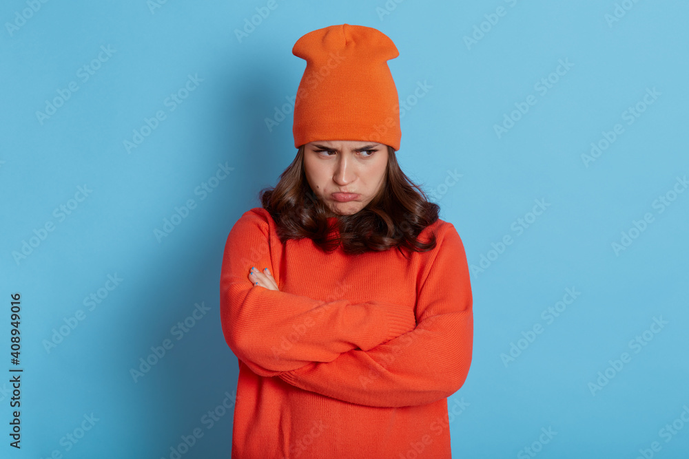 Dark haired caucasian woman stands with arms folded over body, looks ...