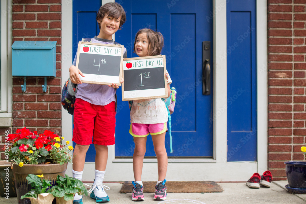 Two siblings stand together on stoop holding First Day of School signs ...