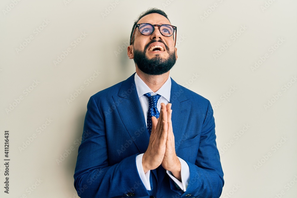 Young man with beard wearing business suit and tie begging and praying ...