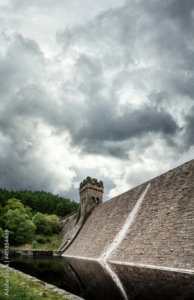 Damn wall with stone overflow tower and green forest in background ...