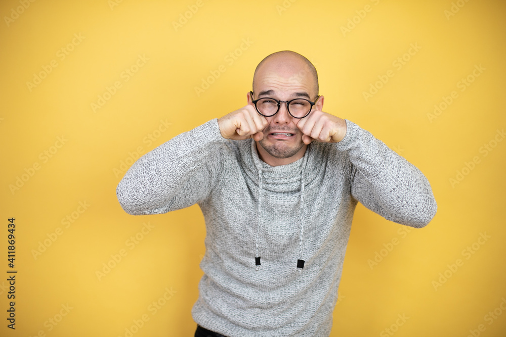 Young bald man wearing glasses over yellow background depressed and ...