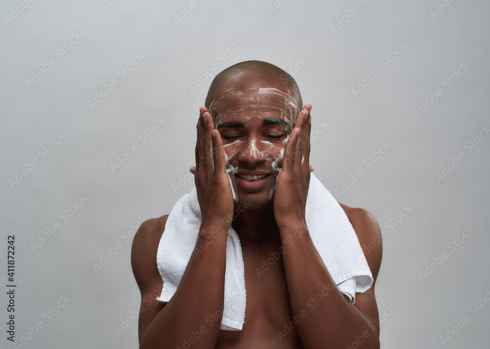 Foto de Stock Shirtless young african american man smiling while washing his face with foam ...