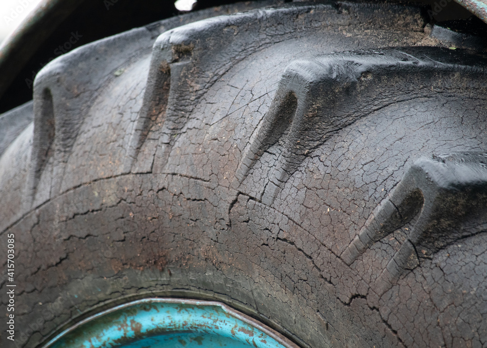 An old tractor tire on dented rim with cracked, worn rubber tread and ...