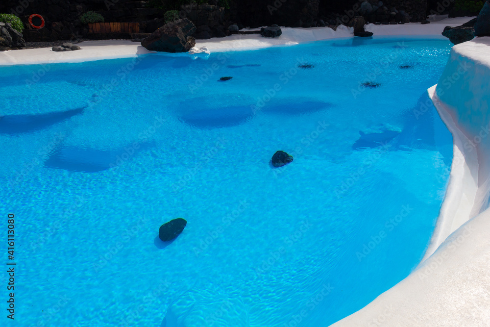 Intense blue swimming pool with volcanic rocks on bottom at Lanzarote ...