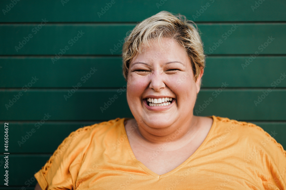Portrait of curvy woman smiling on camera outdoors with green ...