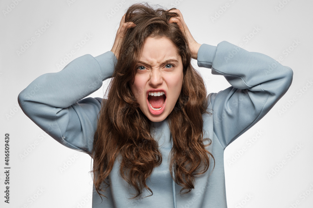 The young woman is angry and screaming, holding her head. Young girl ...