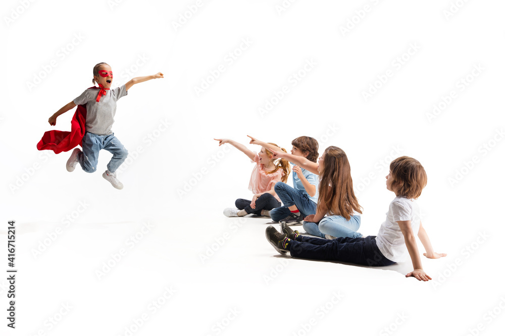 Flying. Child pretending to be a superhero with her friends sitting ...