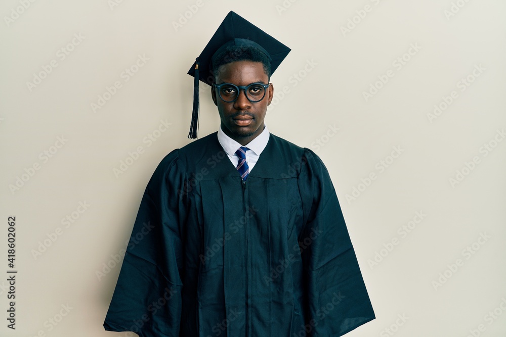 Handsome black man wearing graduation cap and ceremony robe relaxed ...