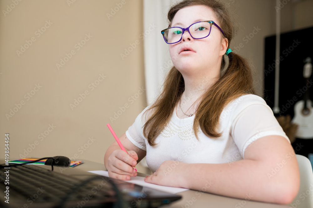 Cute teenager girl with Down syndrome learning online at home. Distance ...
