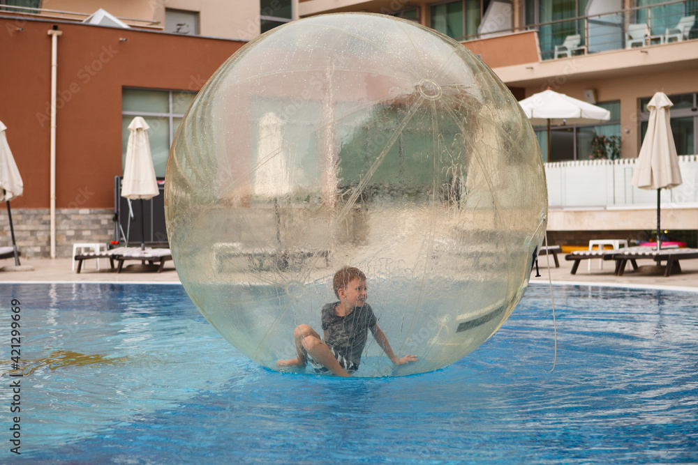 Little boy have fun inside big plastic balloon on the water of swimming ...