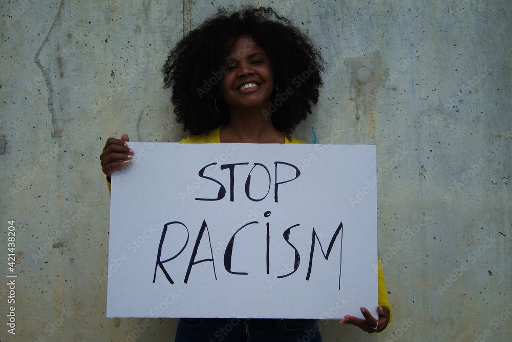 african-american woman holds up a banner reading STOP RACISM. In the ...