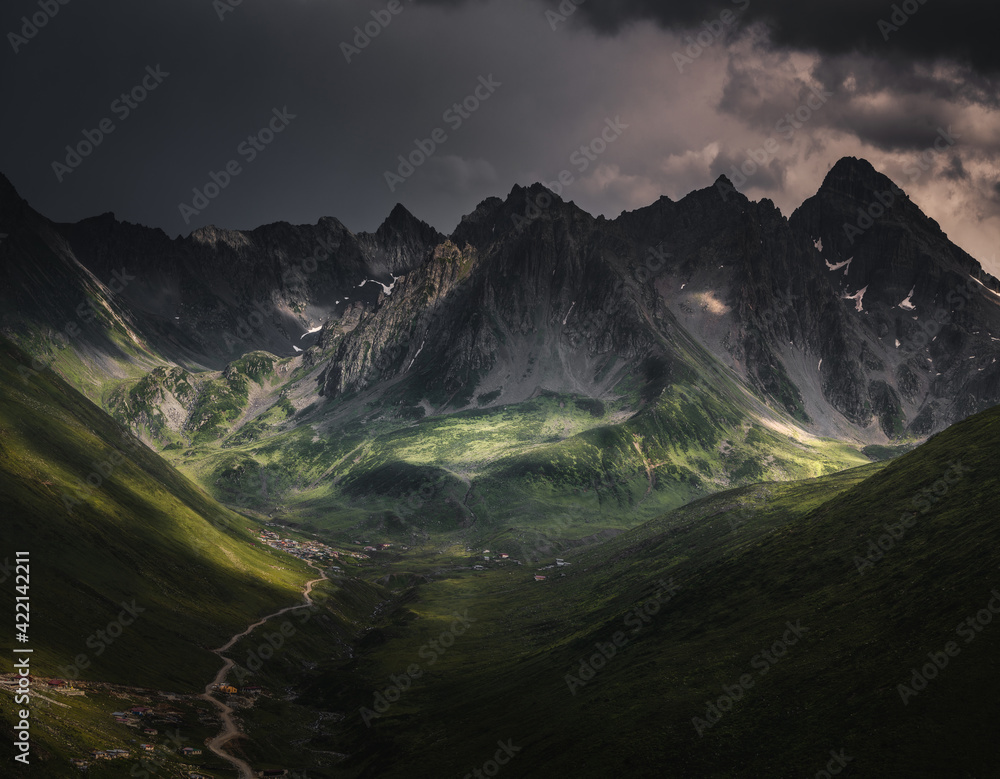 An epic mountain range at the end of a deep valley and a dramatic sky ...