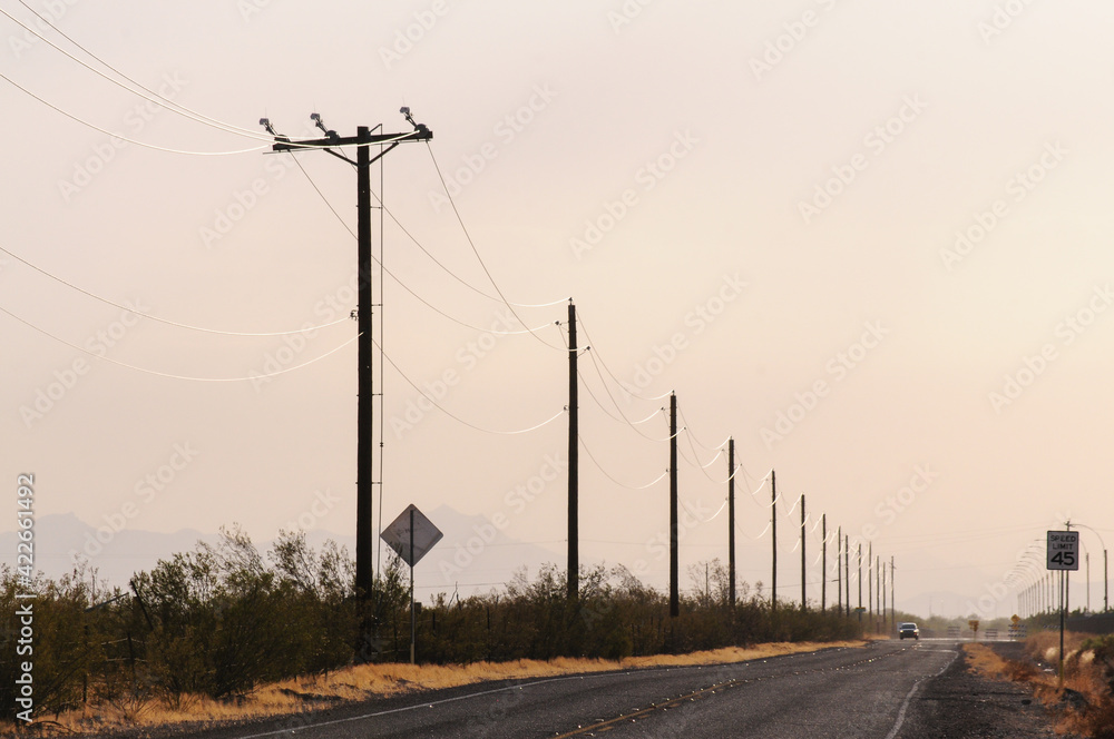 Utility poles with overhead power lines run alongside a rural asphalt ...